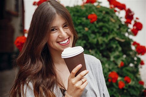 화려한 젊은 여자 커피의 컵을 들고와 꽃의 배경에 거리 시에 웃 고 아름 다운 머리와 완벽 한 미소 시간을 즐기는 행복 Hipster 세련 된 소녀 갈색에 대한 스톡 사진