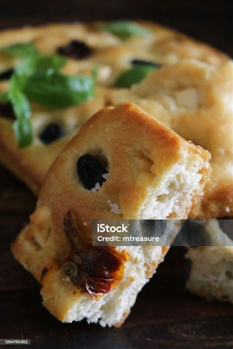 수제 이탈리아 포카치아 빵 덩어리와 슬라이스 녹색 올리브 햇볕에 말린 토마토 바질 잎 장식을 곁들인 페타 치즈를 곁들인 나무 도마의 클로즈업 이미지 전경에 초점을 맞추고