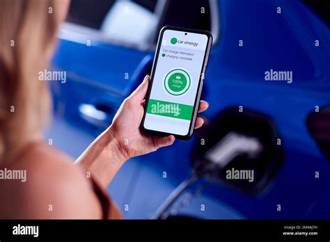 Woman Charging Electric Car With Cable Using App On Phone To Monitor Battery Level Stock Photo
