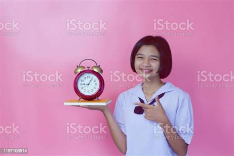 행복 한 아름 다운 젊은 아시아 여자 넣어 알람 시계 와 유니폼 분홍색 배경으로 그녀의 손에 책 Final Round에 대한