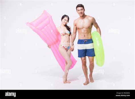 Woman In Bikini Holding A Float And A Man In Swimming Pants Holding A Ring Tube Both Walking