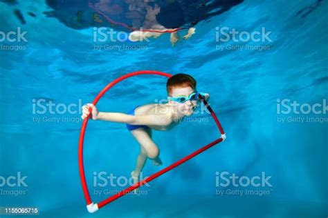 수영장에서 수영하고 바닥에서 수영하는 어린 소년은 장난감을 손에 들고 카메라를 바라보며 빨간 후프를 헤엄치고 있습니다 수중 사진 수평 방향 건강한 생활방식에 대한 스톡 사진