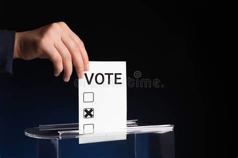 Woman Putting Paper With Word Vote And Tick Into Ballot Box On Dark