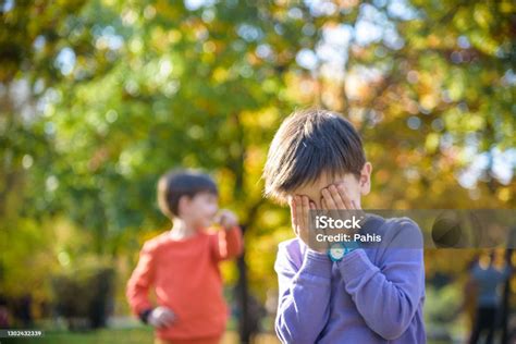 초등학교 마당에서 다른 학생을 괴롭히는 학생 나이가 많은 소년은 어린 아이를 불쾌하게 합니다 등에 웃음 작은 아이는 손과 울음으로 얼굴을 닫고 6 7 살에 대한 스톡 사진