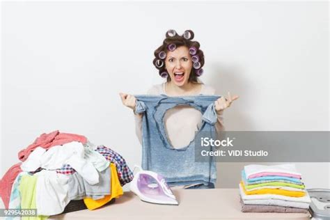 미친 주부 Curlers 들고 가벼운 옷에 머리에 구운 셔츠 다림 질 보드에 서 서 쇠에 의해 만든 구멍 충격된 재미 흰색 배경에 고립 된 여자입니다 광고에 대 한 공간을