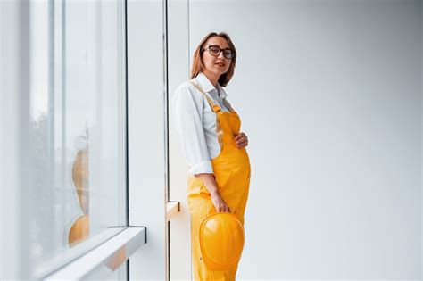 실내에 서 있는 노란 유니폼과 단단한 모자를 쓴 여성 노동자 또는 엔지니어 25 29세에 대한 스톡 사진 및 기타 이미지 25 29세 감정 건축 Istock