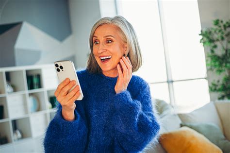 아늑한 방에서 전화기를 들고 낮의 여유로운 시간 동안 기쁨과 흥분을 표현하는 행복한 노인 여성 55 59세에 대한 스톡 사진 및 기타 이미지 Istock