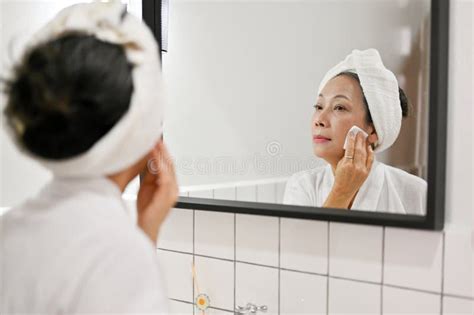 Attractive Mature Aged Asian Woman Removing Makeup Looking In The