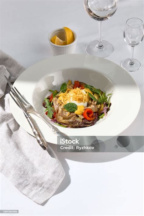 고추냉이 소스와 신선한 녹색 잎을 곁들인 쇠고기 혀 샐러드 드레싱 흰색 테이블에 은제품이 있는 화이트 레스토랑 접시와 유리가 놓인 화이트 레스토랑 접시 야채와 고기 샐러드