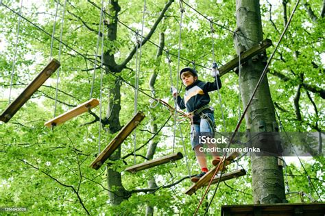 숲 모험 공원에서 학교 소년 헬멧을 쓰고 있는 아이는 높은 로프 트레일에서 올라간다 민첩성 기술과 어린이를위한 야외 놀이 센터를 등반 어린이 및 가족을위한 야외 활동 고등