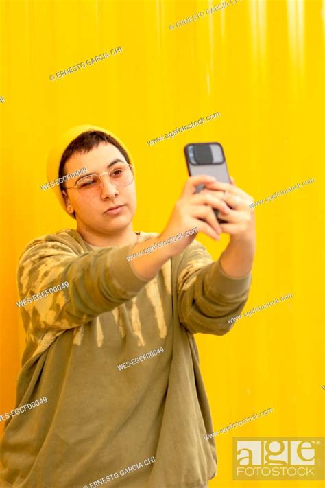 Non Binary Person Taking Selfie Through Smart Phone In Front Of Yellow