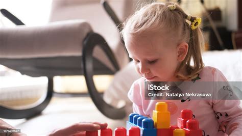 웃고 있는 어린 아이 화려한 큐브를 가지고 노는 금발의 미취학 아동 분홍색 잠옷을 입고 바닥에 앉아 집에 큰 창문이 있는 햇볕이 잘 드는 방 아이들의 초기 발달 2 3 살에