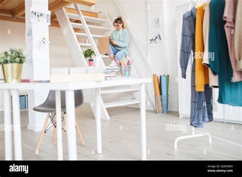 Serious Busy Young Female Designer Of Fashionable Clothes Sitting On