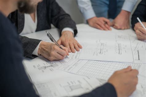 Close Up Of The Hands Of Four Colleagues With Blueprints On The Table In The Office