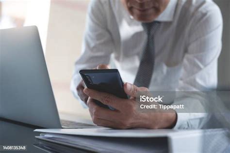현대 사무실의 테이블에 비즈니스 문서가있는 랩톱 컴퓨터에서 작업하는 모바일 스마트 폰을 사용하는 사업가 남자 사업가에 대한 스톡