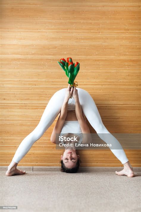 흰색 정장 하 고 서 걸쳐져 앞으로 벤드 포즈 Prasarita Padottanasana 요가 연습에 발랄 한 젊은 여자의 전체 길이 전면 보기 보유 튤립