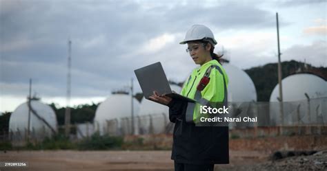 흰색 안전모를 쓴 노트북을 사용하는 산업 엔지니어 여성이 정유 공장 앞에 서 있습니다 공장 석유 저장 탱크 및 파이프 라인 정유 공장의 노동자 가솔린에 대한 스톡 사진 및