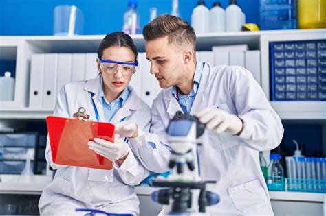 Man And Woman Scientists Using Microscope Write On Clipboard At
