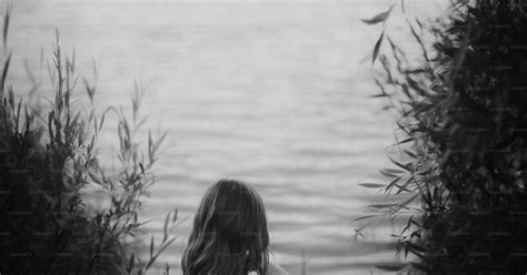 호수 근처의 일몰 빛에 모래 해변에 앉아 슬픈 소녀 물 근처에 바람이 부는 머리를 가진 흰색 보헤미안 드레스를 입은 젊은 여성의 뒤 외로움과 우울증 개념 사진