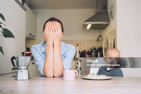 어린 아기와 함께 일하는 어머니 부엌에서 아침 식사를 하는 커피와 아기를 가진 젊은 피곤한 여자 현대 프리랜서 엄마와 그녀의 아이는 불면의 밤 후 일과 삶의 균형 또는 일과
