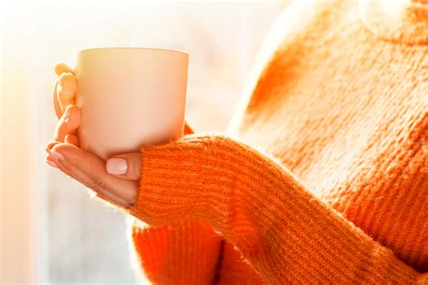 한 여성이 집에서 창문을 통해 일출과 함께 커피를 마십니다 여자 손을 닫고 집에서 창 근처 뜨거운 커피 컵을 들고 있다 가을에