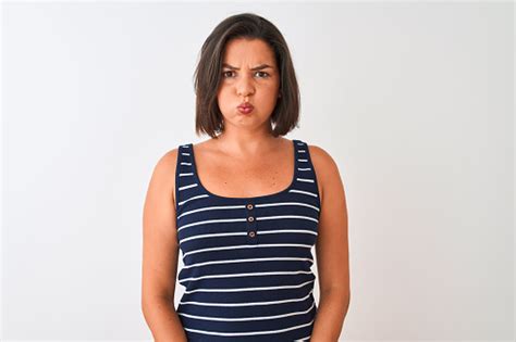 젊은 아름다운 여자는 재미있는 얼굴과 고립 된 흰색 배경 퍼핑 뺨 위에 서 파란색 줄무늬 티셔츠를 입고 공기 미친 표정으로 입이 팽창 T 셔츠에 대한 스톡 사진 및 기타