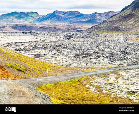 A Road Winds Beside A Vast Solidified Lava Field Under A Cloudy Sky