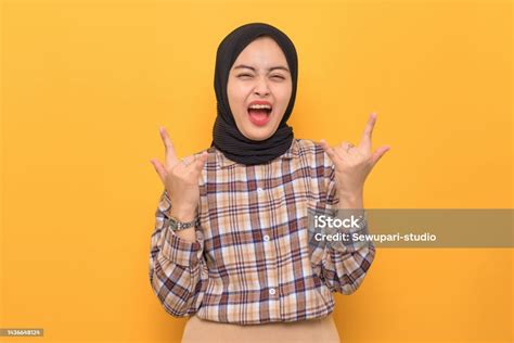 격자 무늬 셔츠를 입은 흥분한 젊은 아시아 여성이 노란색 배경에 고립 된 록 기호를하는 미친 표정으로 외치고 있다 20 24세에 대한 스톡 사진 및 기타 이미지 Istock