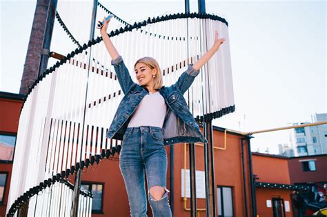 스마트 폰 기술을 들고 카메라를 비웃는 손을 들고 행복한 힙스터 소녀의 절반 길이 초상화 청바지 의류를 입은 쾌활한 백인 여성이 현대 도시 도시에서 기뻐합니다 25 29세에