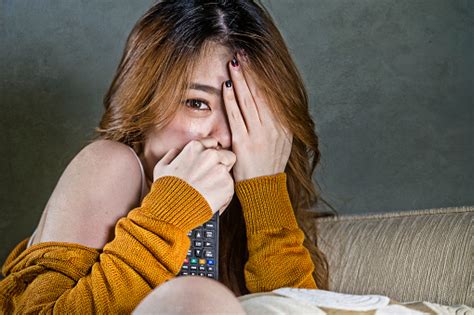 젊은 매력적이 고 귀여운 무서 워 아시아 한국 여자 보고 공포 영화 또는 Tv 드라마 지주 리모컨 두려움과 공황 얼굴 표현에 집 거실 소파에서 혼자 Brand Name