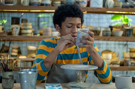 재능 있는 젊은 아프리카계 미국인 소년이 워크숍 스튜디오에서 앞치마를 두르고 손으로 진흙과 점토로 냄비와 조각품을 능숙하게 만들어 예술적 비전을 실현합니다 14 15 살에