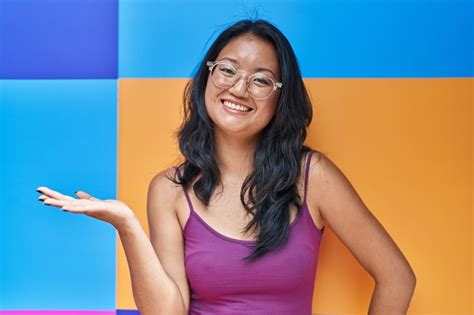 행복한 미소와 승자 표현으로 성취를 축하하는 화려한 배경 위에 서 있는 아시아 젊은 여성 갈색 머리에 대한 스톡 사진 및 기타 이미지 갈색 머리 긍정적인 감정 표현