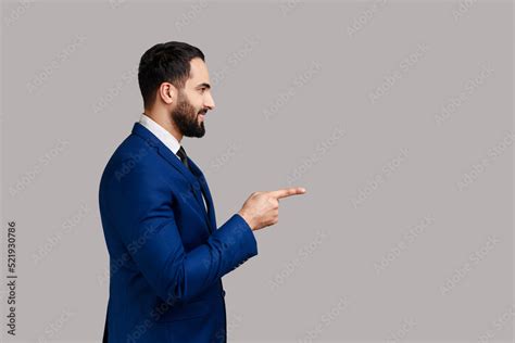 Side View Of Bearded Man Pointing Finger Away With Toothy Smile On Face