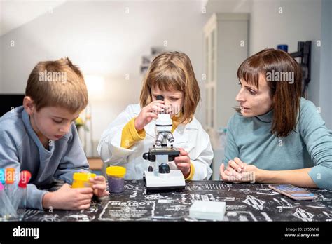 Girl Looking Through Microscope Amidst Brother And Mother At Home Stock