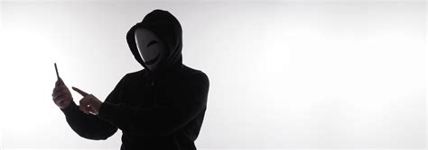 Hacker Anonymous And Face Mask With Smartphone In Hand Man In Black Hood Shirt Holding And