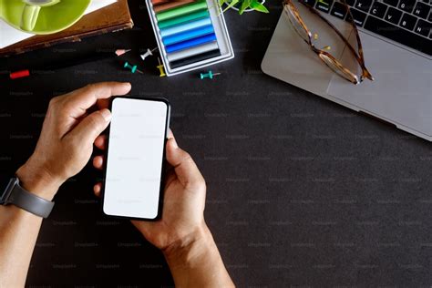 어두운 사무실 책상에서 사무용품과 함께 스마트폰 모형을 사용하는 사업가 손의 자른 샷 평면도 그래픽 디스플레이 몽타주를 위한 빈 화면 휴대폰 사진 Unsplash의 빈