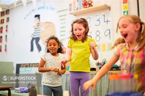 Primary Schoolgirls Fooling Around In Classroom Superstock