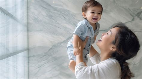 질감 있는 대리석 벽 배경에서 기쁨으로 아들을 안고 웃고 있는 아시아 어머니 엄마 아들 귀여운 가족 아시아 부모 배경