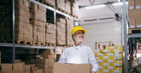 창고에서 상자를 들고 웃고 있는 여성 노동자 머리에 보호 헬멧 선반에있는 상자 주위 사진 Unsplash의 보관실 이미지