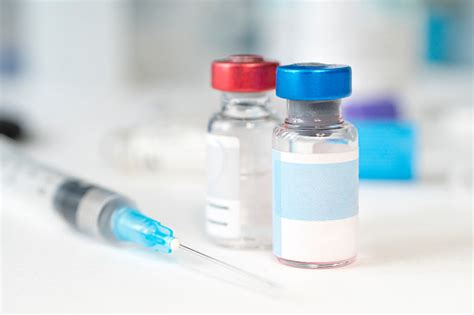 파란색 그라데이션 배경이있는 흰색 테이블에 주입을위한 빈 라벨 의료 유리 유리 및 플라스틱 주사기 예방 접종 당뇨병 및 미용