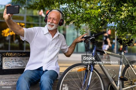 잘생긴 중년 남자가 자전거를 타고 시내에 가서 옆에 서서 스마트 폰으로 셀카를 찍습니다 60 69세에 대한 스톡 사진 및 기타