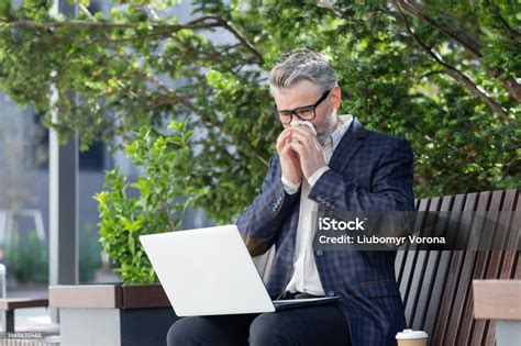 백발의 성숙한 남자는 공원 벤치에 앉아 재채기를하고 사업가는 야외에서 노트북으로 일하고 감기와 알레르기로 아프다 45 49세에 대한 스톡 사진 및 기타 이미지 Istock