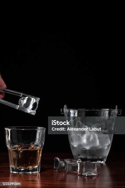 레스토랑의 나무 테이블에 알코올 음료 뒤에 위스키 얼음 양동이와 유리 위에 얼음 큐브를 들고 집게와 손 복사 공간에 대한 검은색