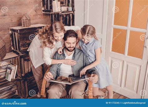 Daughter Mother And Father Sitting In Rocking Chair And Reading Book