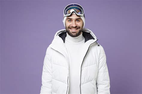 따뜻한 흰색 패딩 윈드 브레이커 재킷 스키 고글 마스크에 미소 스키어 남자는 보라색 배경에 고립 된 산에서 극단적 인 주말 겨울 시즌을 보낼 것입니다 사람들 라이프 스타일