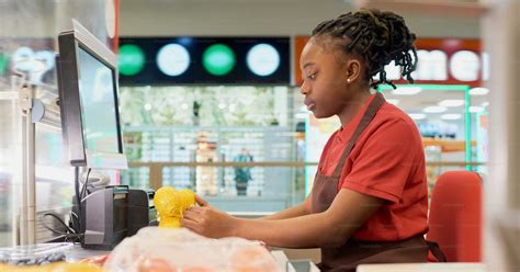 유니폼을 입은 젊은 여성 상점 조수가 카운터에 앉아 슈퍼마켓에서 고객에게 서비스를 제공하는 동안 가방에 담긴 신선한 레몬을 스캔합니다 사진 Unsplash의 러시아 이미지
