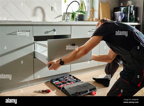 Man Assembling Kitchen Drawer In Modern Cabinet Using Screwdriver