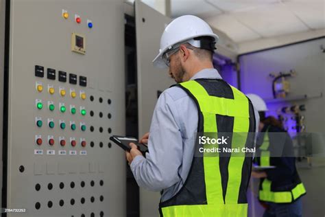 공장의 주 전기 제어실에서 컴퓨터와 디지털 태블릿으로 작업하는 두 명의 백인 백인 전문 전기 기술자 Mdb 주 배전반 2명에