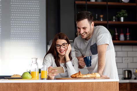 부엌에서 부부는 손에 미소에 휴대 전화와 테이블에서 오렌지 주스와 페이스트리와 아침 식사를 먹는다 2명에 대한 스톡 사진 및 기타 이미지 Istock