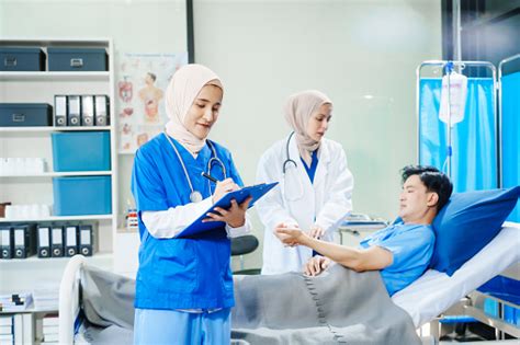 두 명의 무슬림 여성 의사가 병원에서 수술 후 침대에 누워 있는 남성 환자의 병력과 증상을 확인하고 회복 및 건강 상태를 모니터링합니다 3 명에 대한 스톡 사진 및 기타